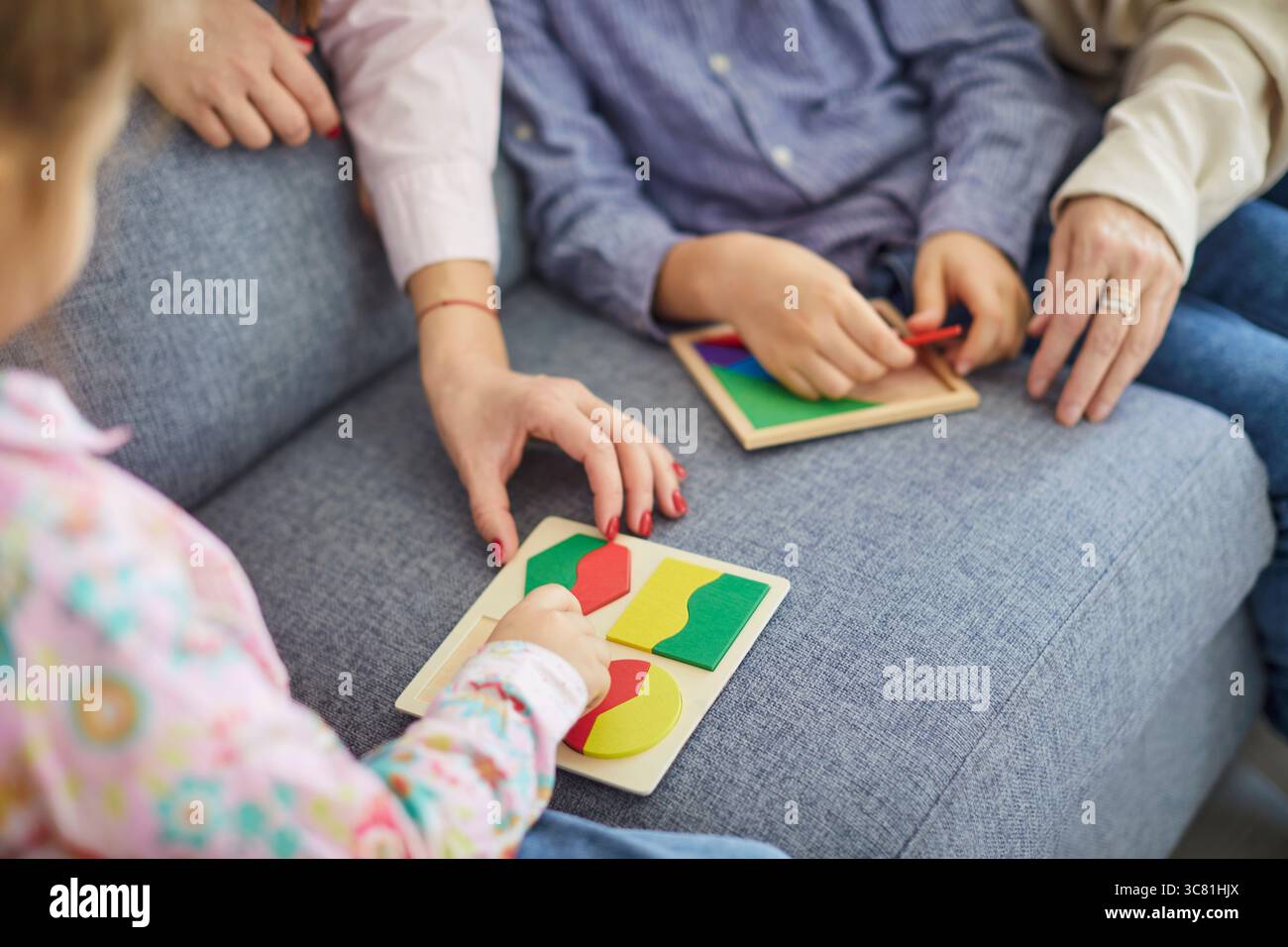 Children playing with colorful jigsaw puzzle on sofa while adults ...