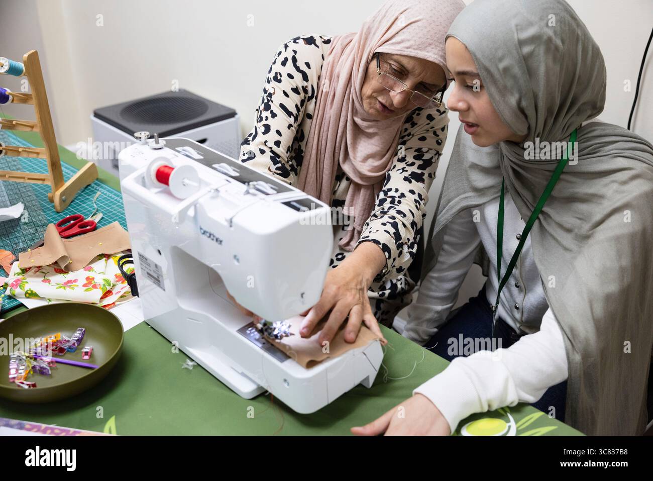 Amal Alalim helps Jenine Zatar, 14, in a sewing class at Olive ...