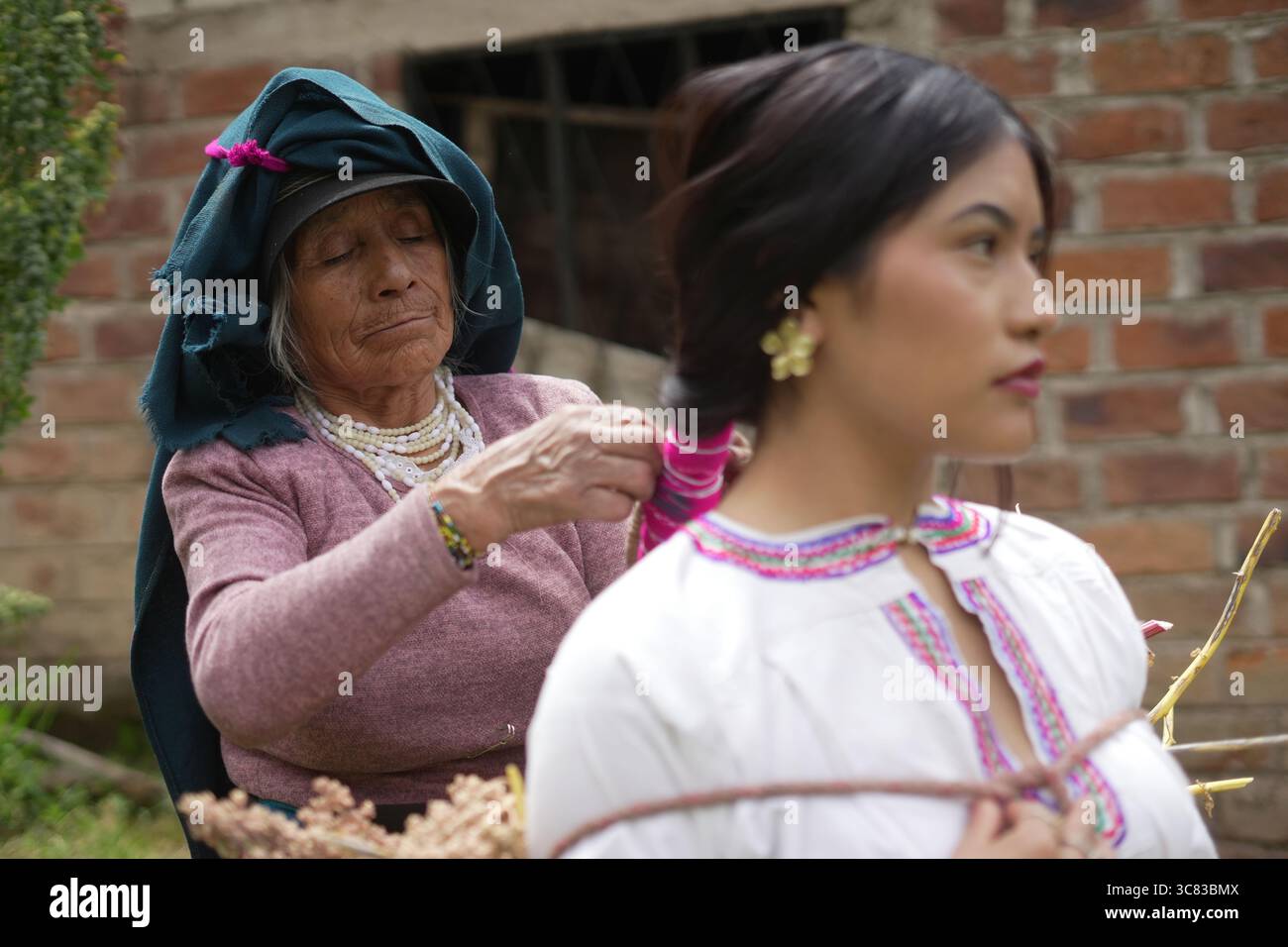 Indigenous woman gently braiding hair of younger female wearing ...