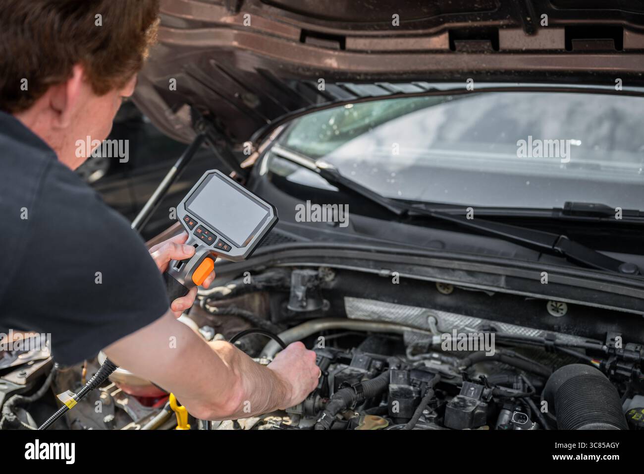 Mechanic using diagnostic tool to inspect car engine during vehicle ...