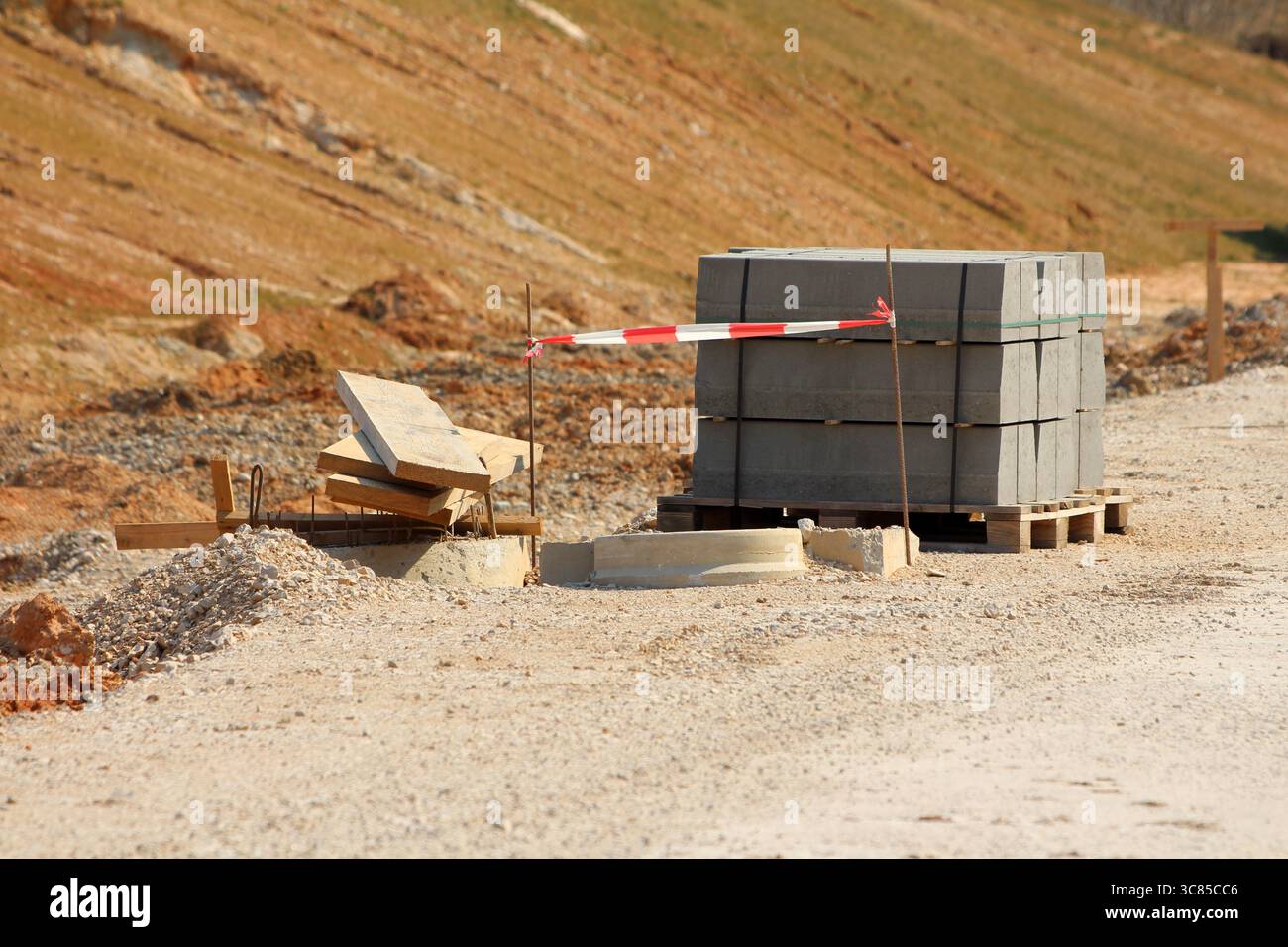 Concrete curb segments are laid along a gravel road while pallets of ...