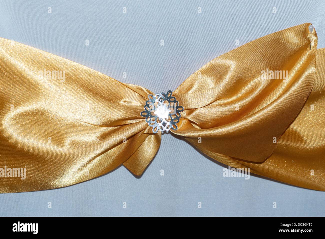 A golden satin bow featuring a decorative brooch is displayed ...