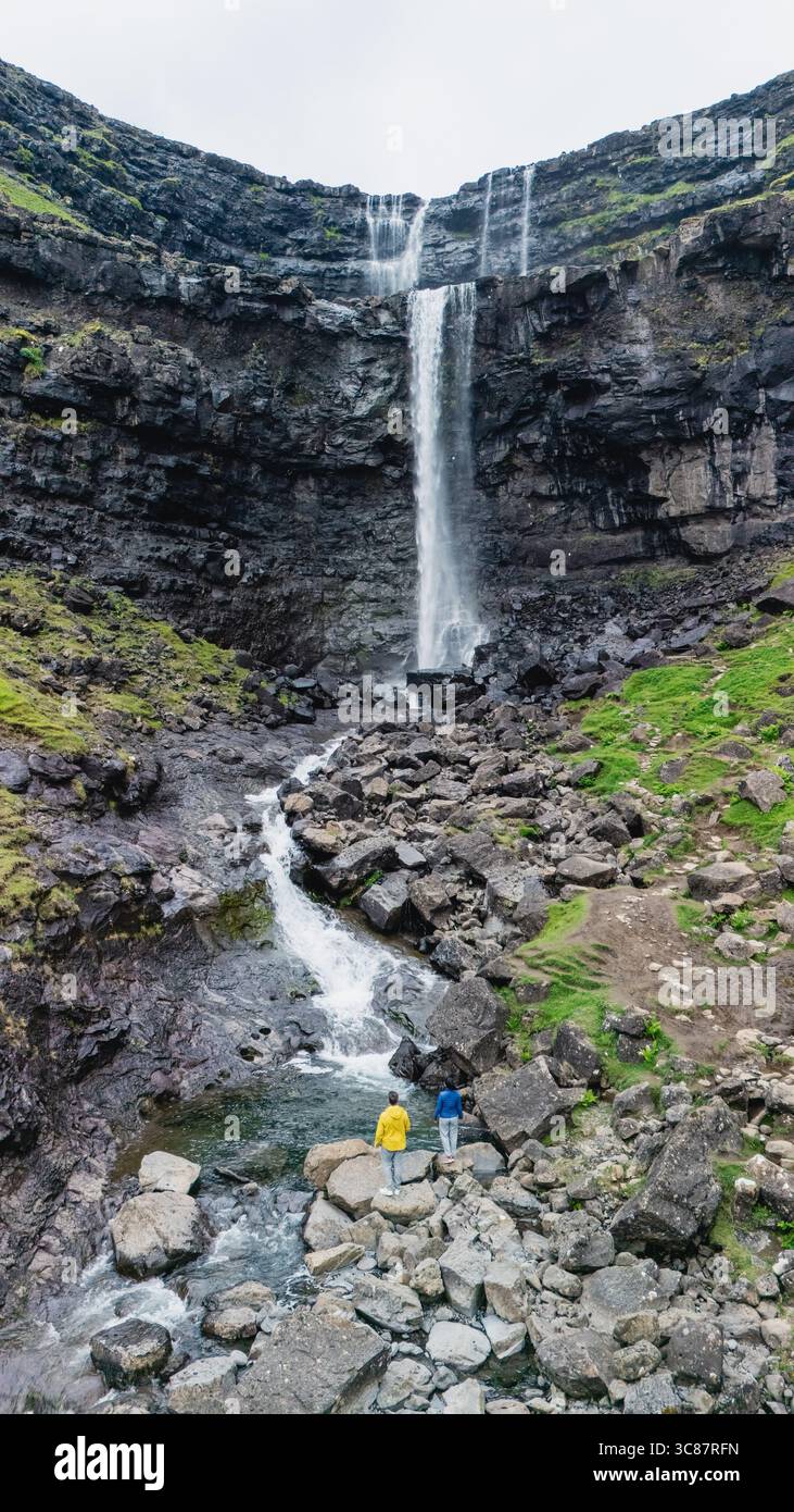 Nestled in the Faroe Islands, adventurers stand in awe of a majestic ...