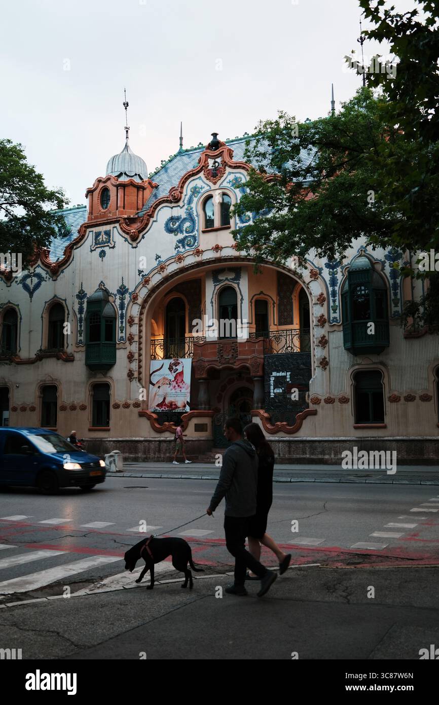 People walking a dog in front of Raichle Palace during a calm evening ...