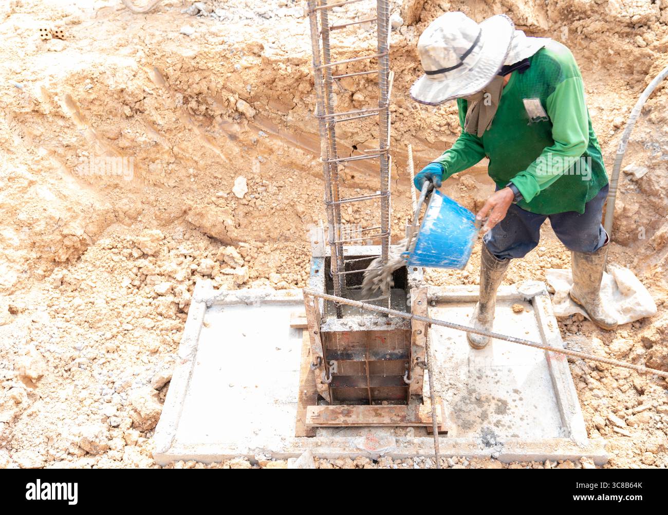 A construction worker is pouring concrete manually into a column ...
