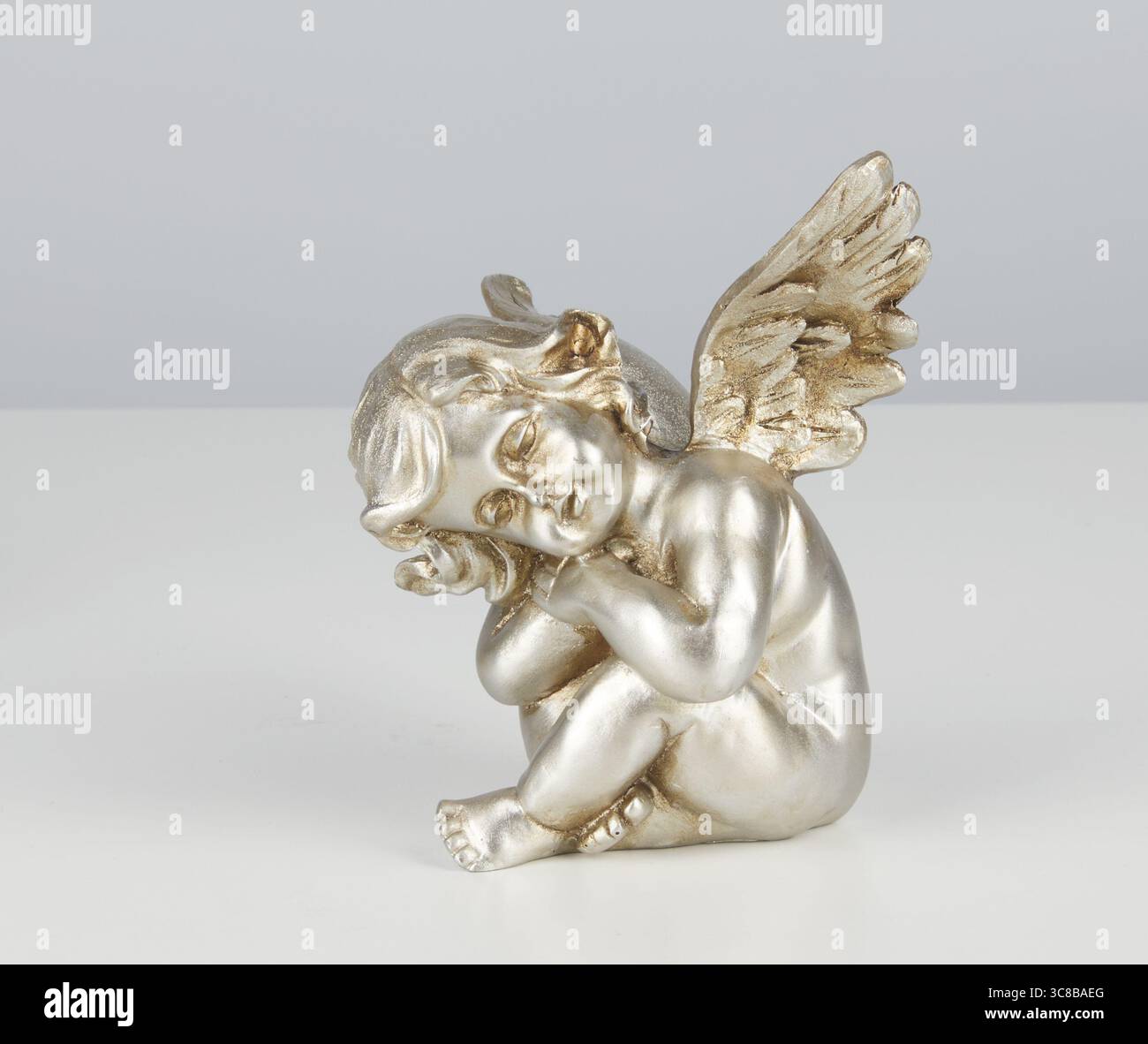 Golden ceramic little angel in a sitting position, hugging her chest ...