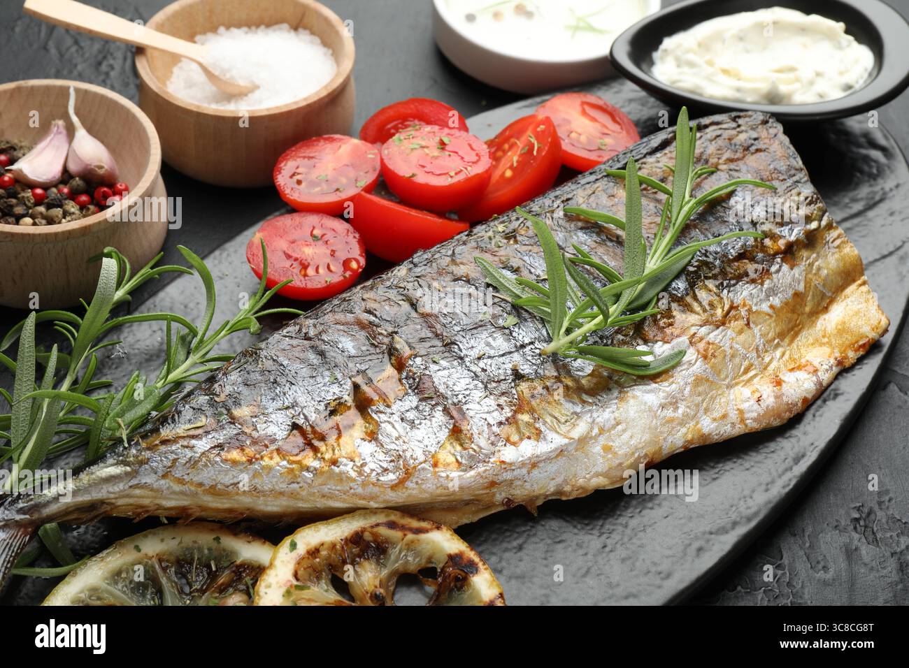 Tasty roasted mackerel served with spices and sauce on black table ...