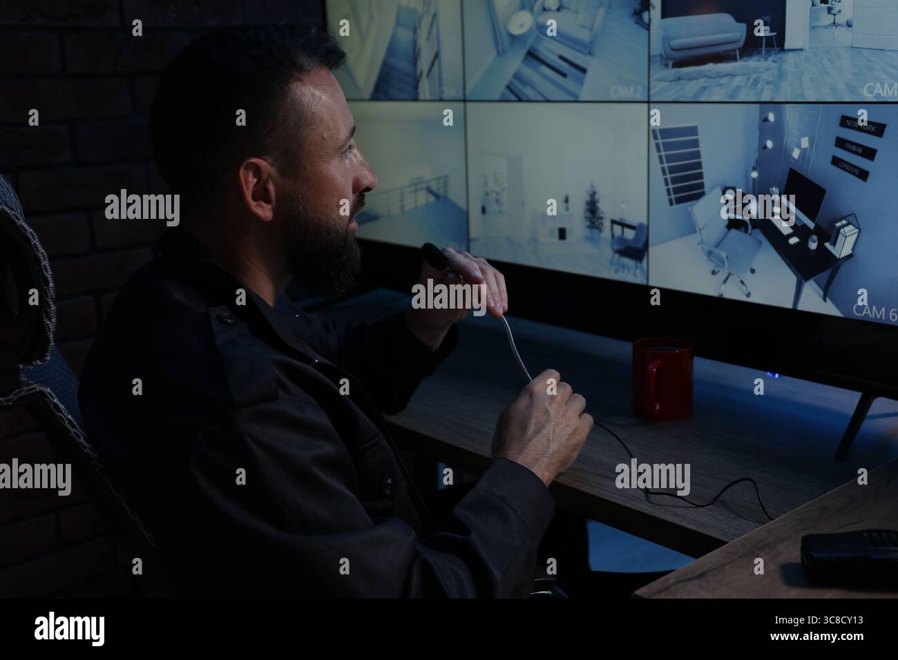 Security guard monitoring CCTV cameras and using microphone in office ...