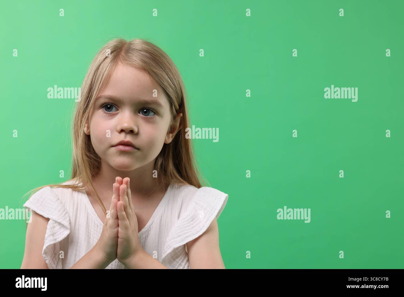 Little girl with clasped hands apologizing on green background. Space ...