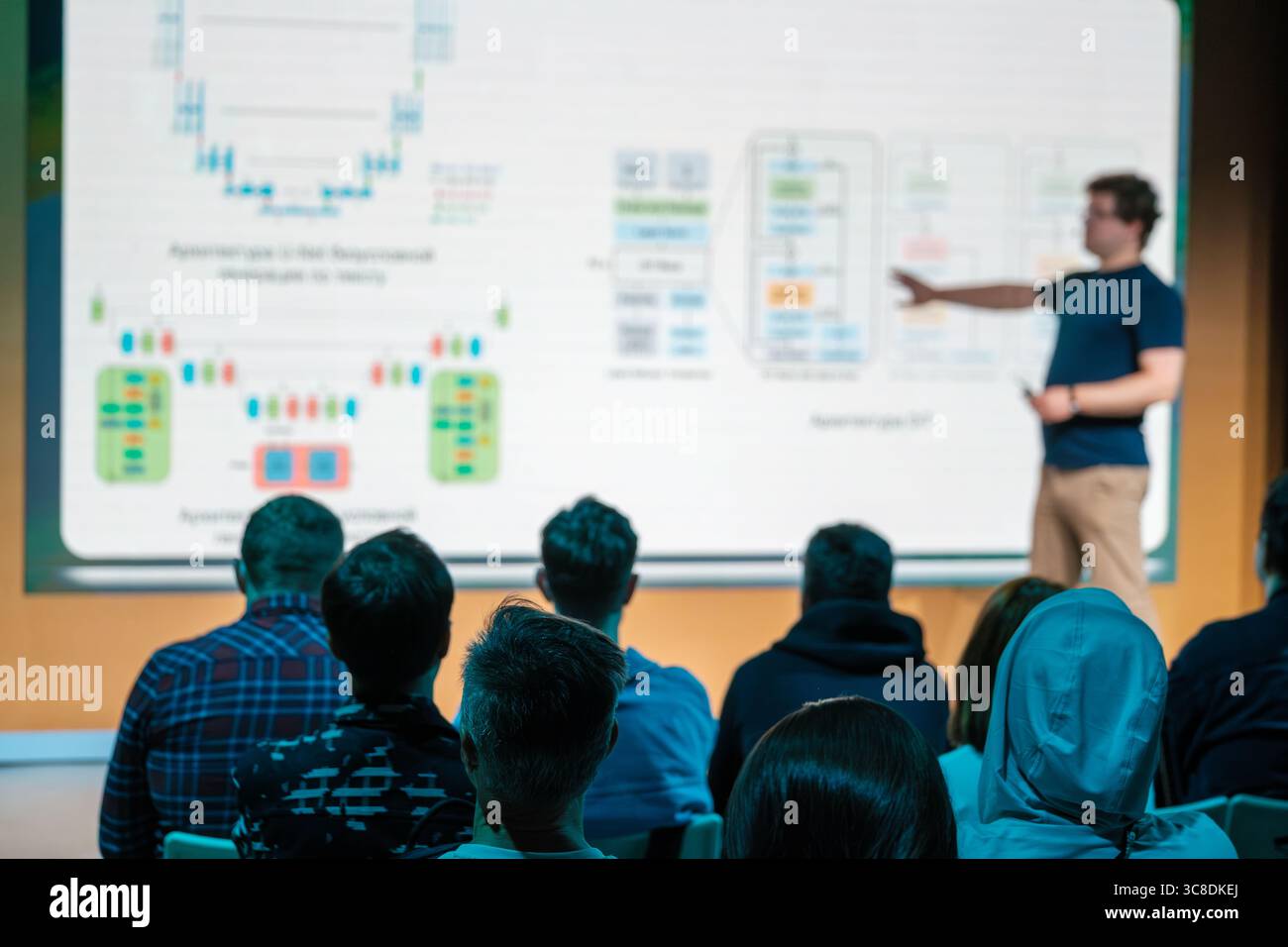 Audience listens to presenter explaining a schematic diagram on a large ...