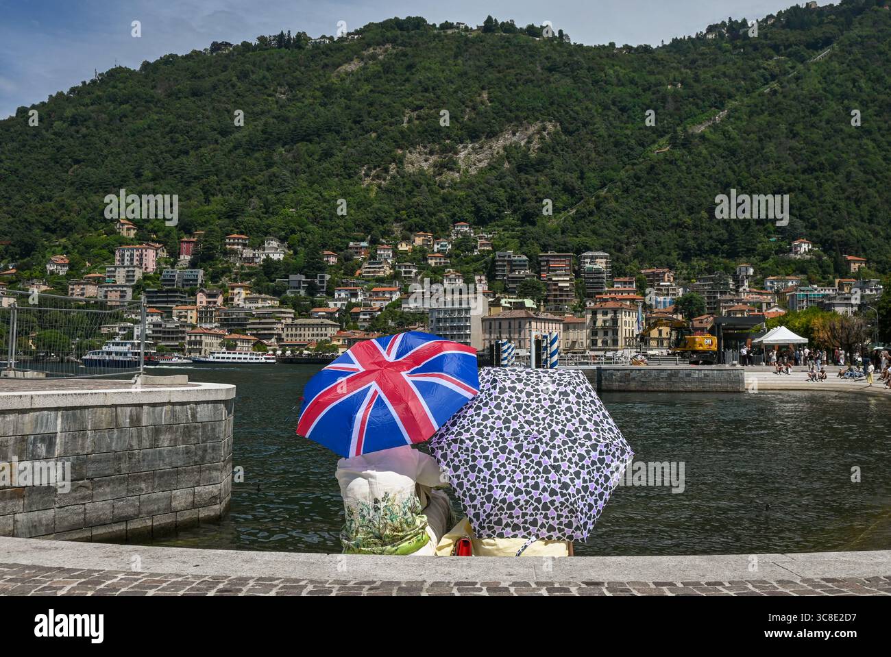 two woman with umbrellas sitting on the banks of Lake Como in Como ...