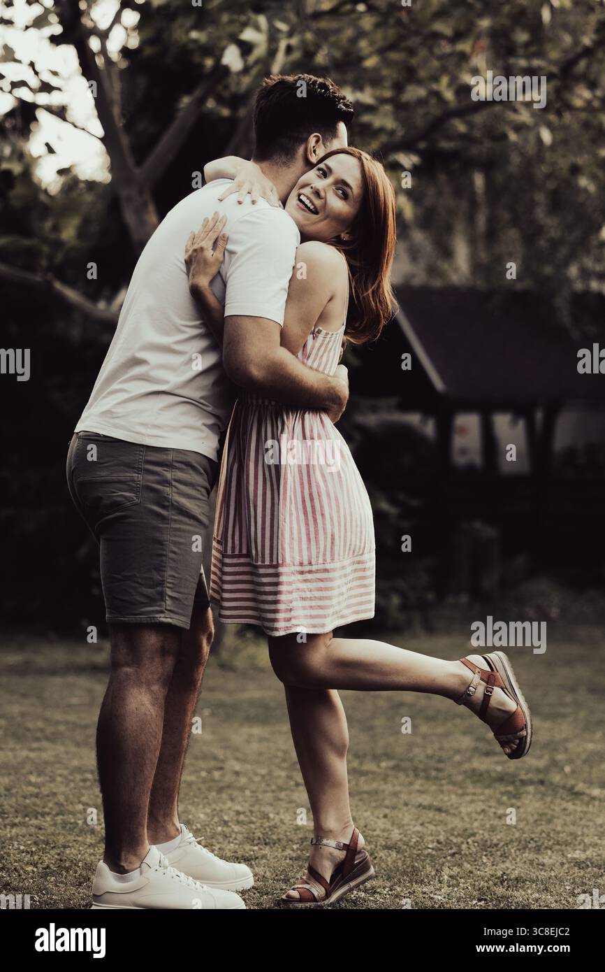 Pretty smiling woman hugging her boyfriend in nature, holding one leg ...