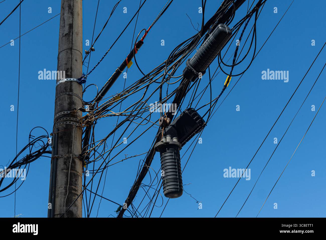 A power pole with a tangle of wires and cables against a blue sky ...