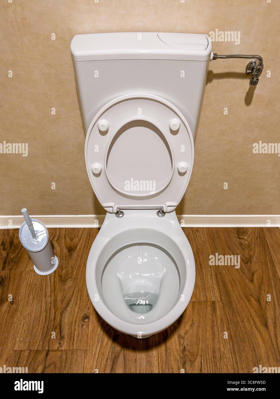 White toilet bowl with open lid and flush tank on brown wall and wooden ...