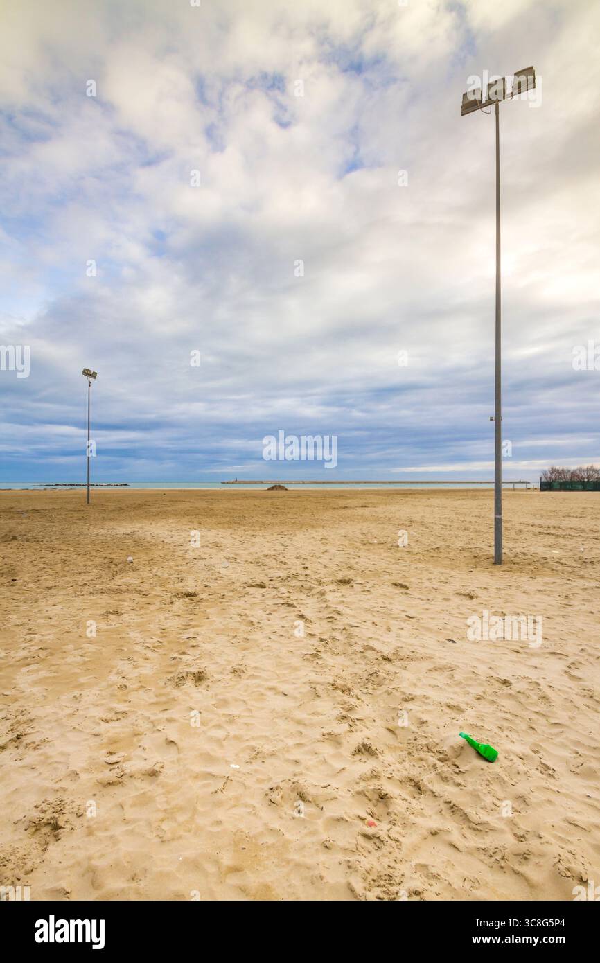 Sandy beach polluted with plastic debris, light poles, cloudy sky ...