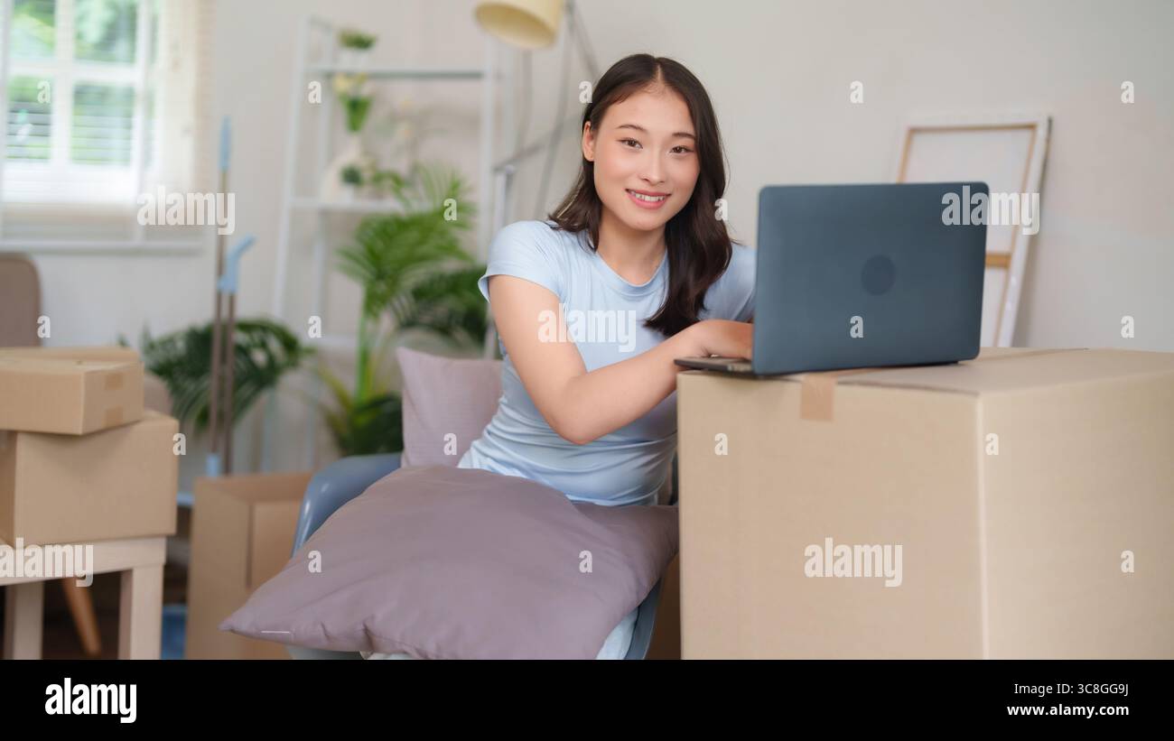 Asian adult woman happily uses computer planning new apartment ...