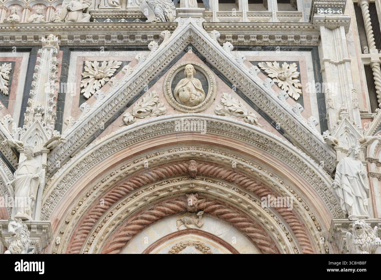 Detail of pointed gable, statues, and arches on the right portal of Siena Cathedral (Duomo di ...