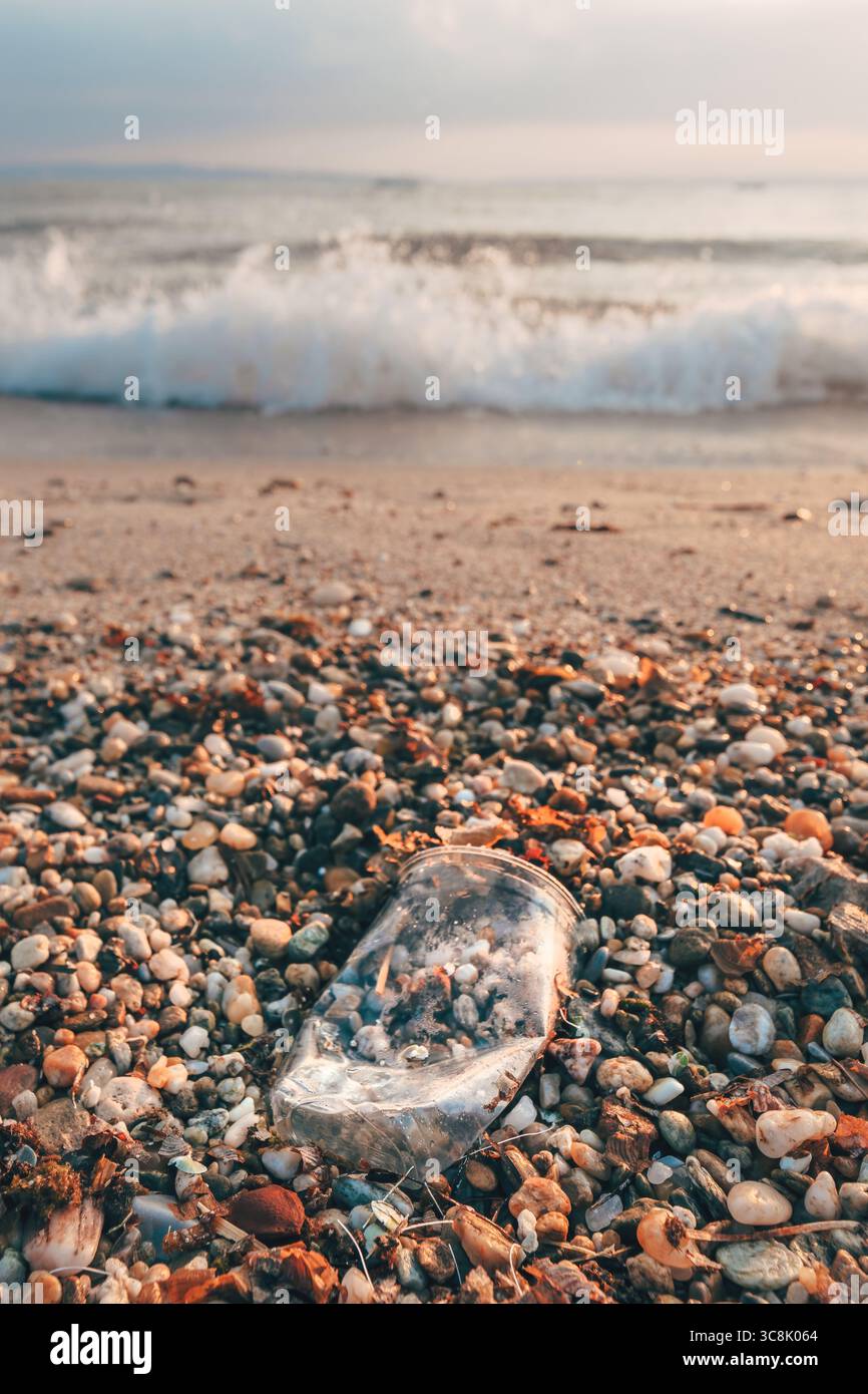 Plastic bottle waste on a pebble beach with ocean waves in the ...