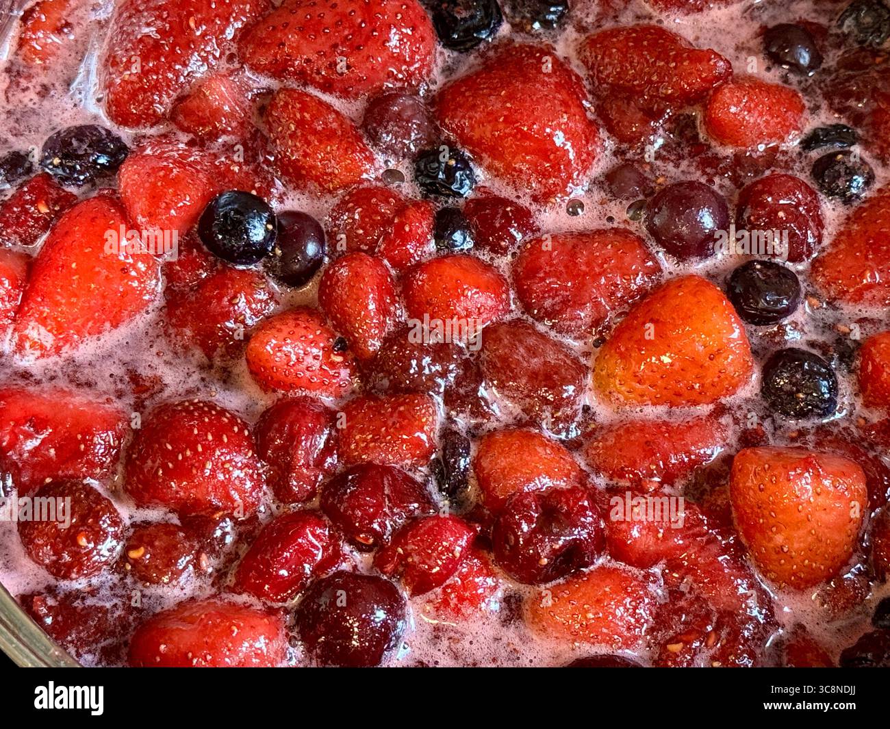 Various red berries are boiling in a pot. Homemade jam making process ...
