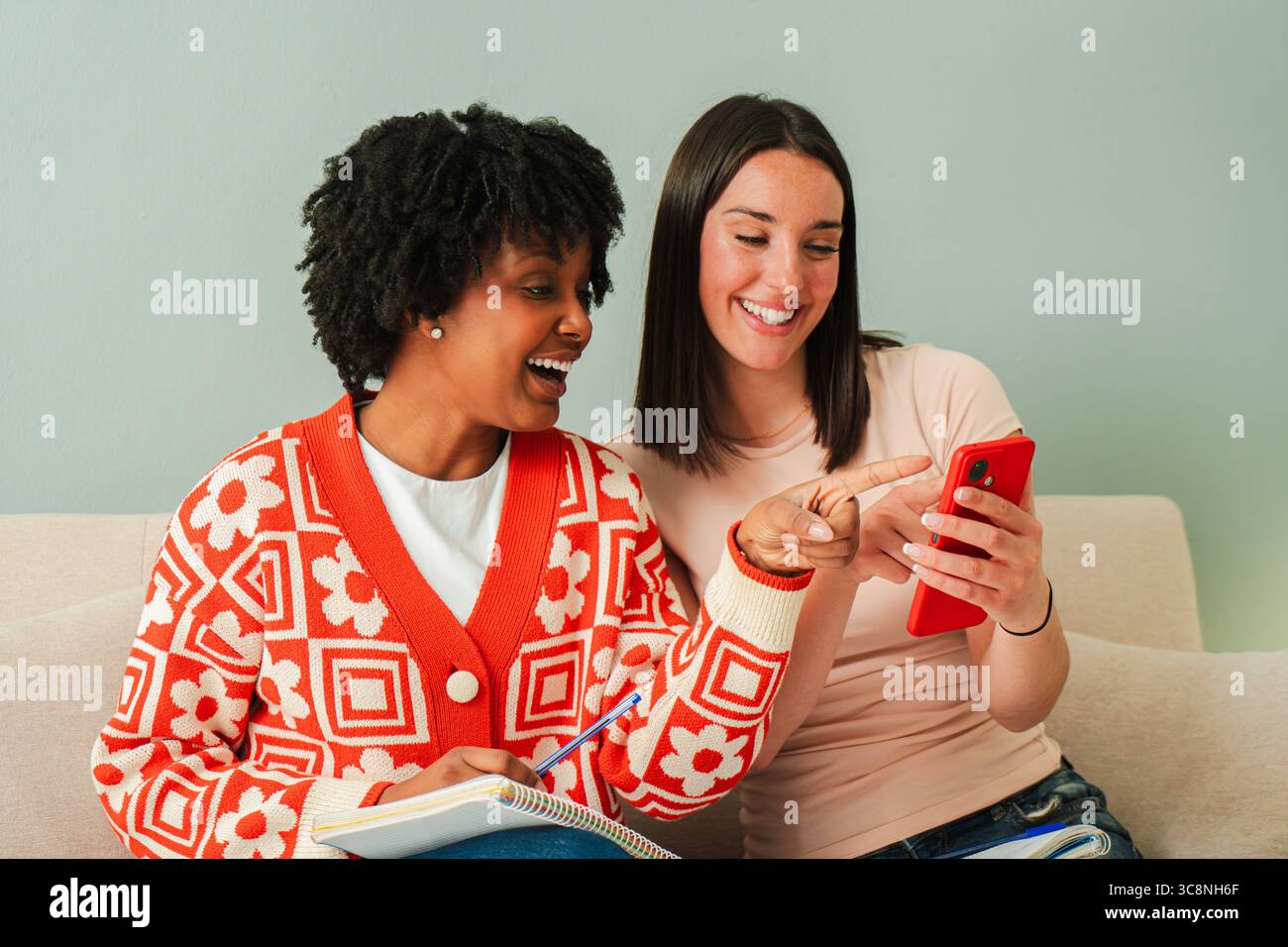 Two enthusiastic females happily interacting with a smartphone, sharing ...