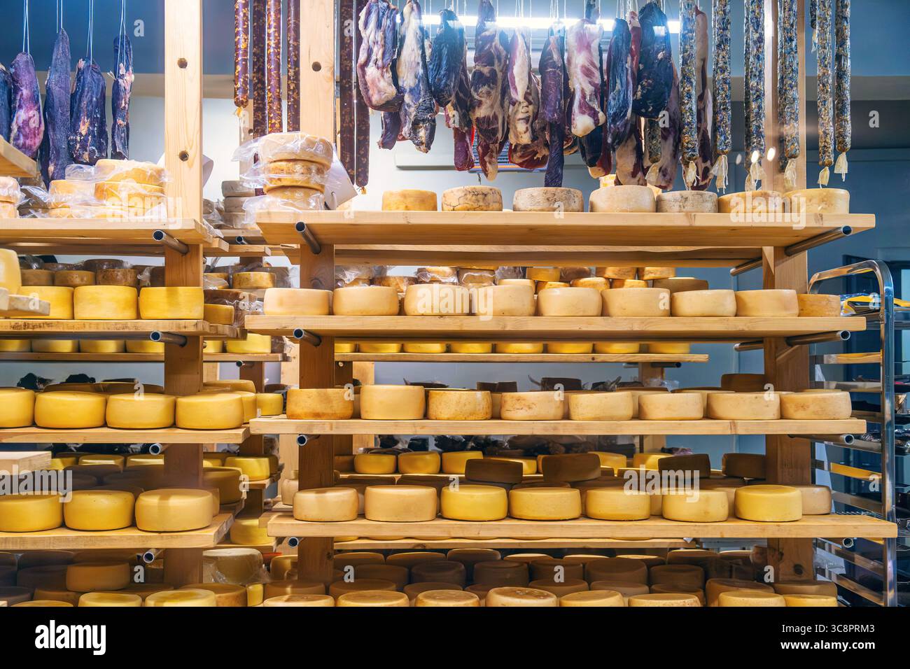Cheese wheels aging on wooden shelves in cheese cellar with hanging ...