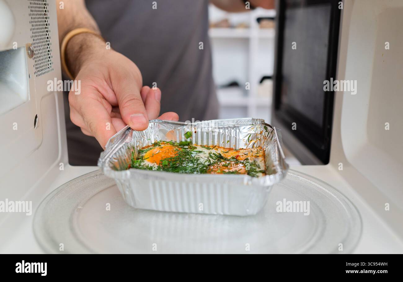 Person placing ready-to-eat meal in aluminum tray into a microwave oven ...