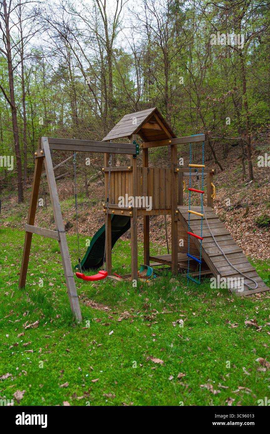 Wooden playground set with swing, slide, and climbing rope in forest ...