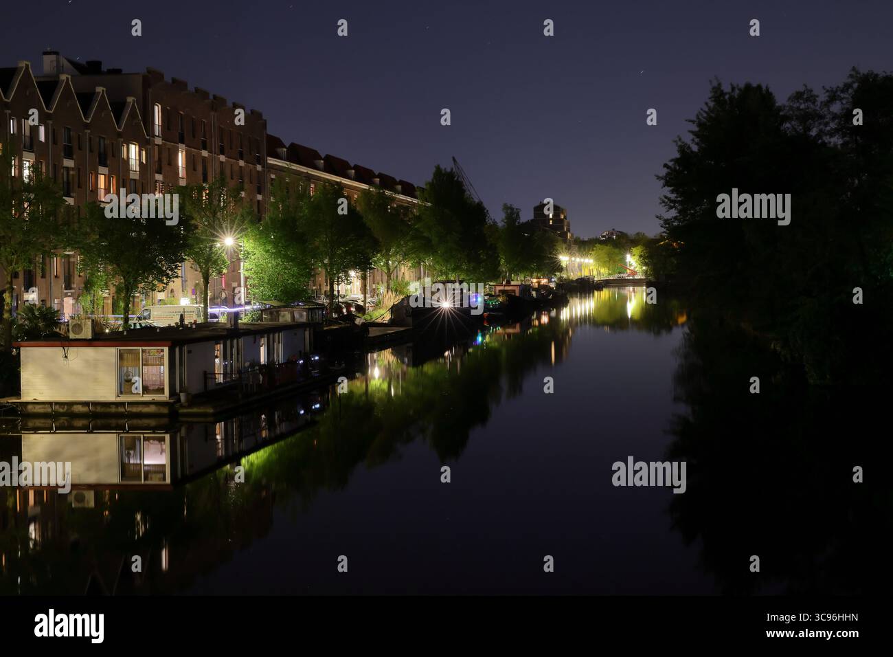 Soft amber streetlights illuminate Amsterdam’s Entrepotdok canal at ...
