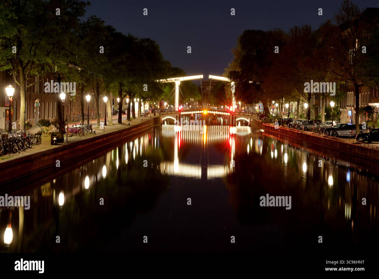 Golden lights trace the silhouette of Walter Suskindbrug drawbridge over reflective Amsterdam ...