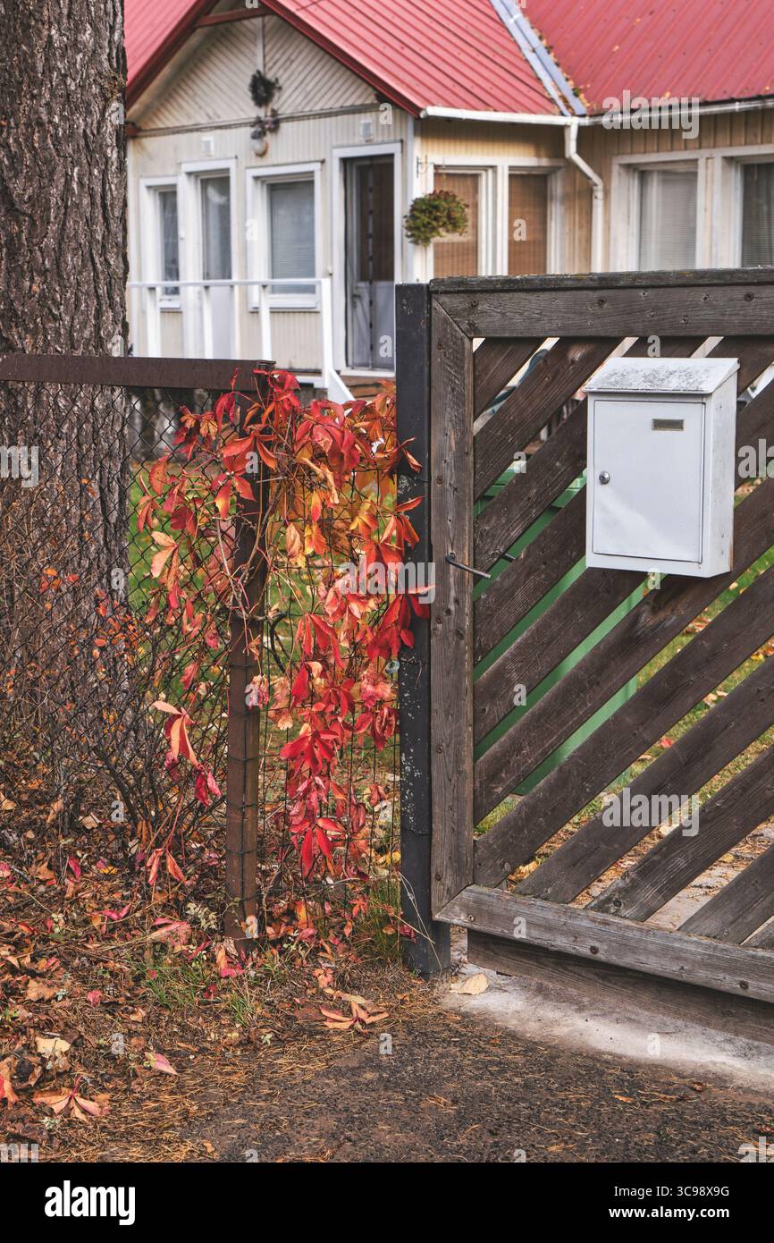 Wooden gate with mailbox and red autumn leaves near cozy countryside ...
