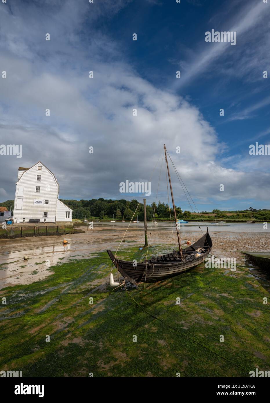 Old wooden boat with mast sitting on mud. Old tide mill behind. View of ...