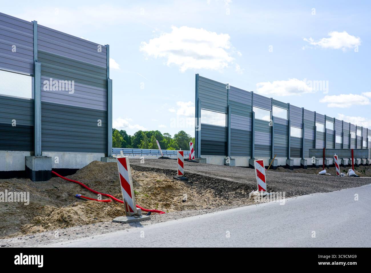 A section of a highway shows partially completed noise barriers, red ...