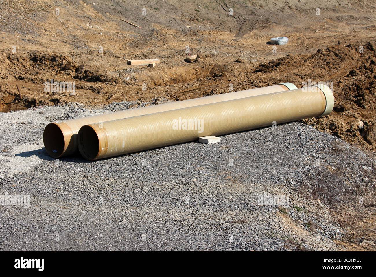 Two large beige fiberglass pipes rest on gravel in an active earthwork ...