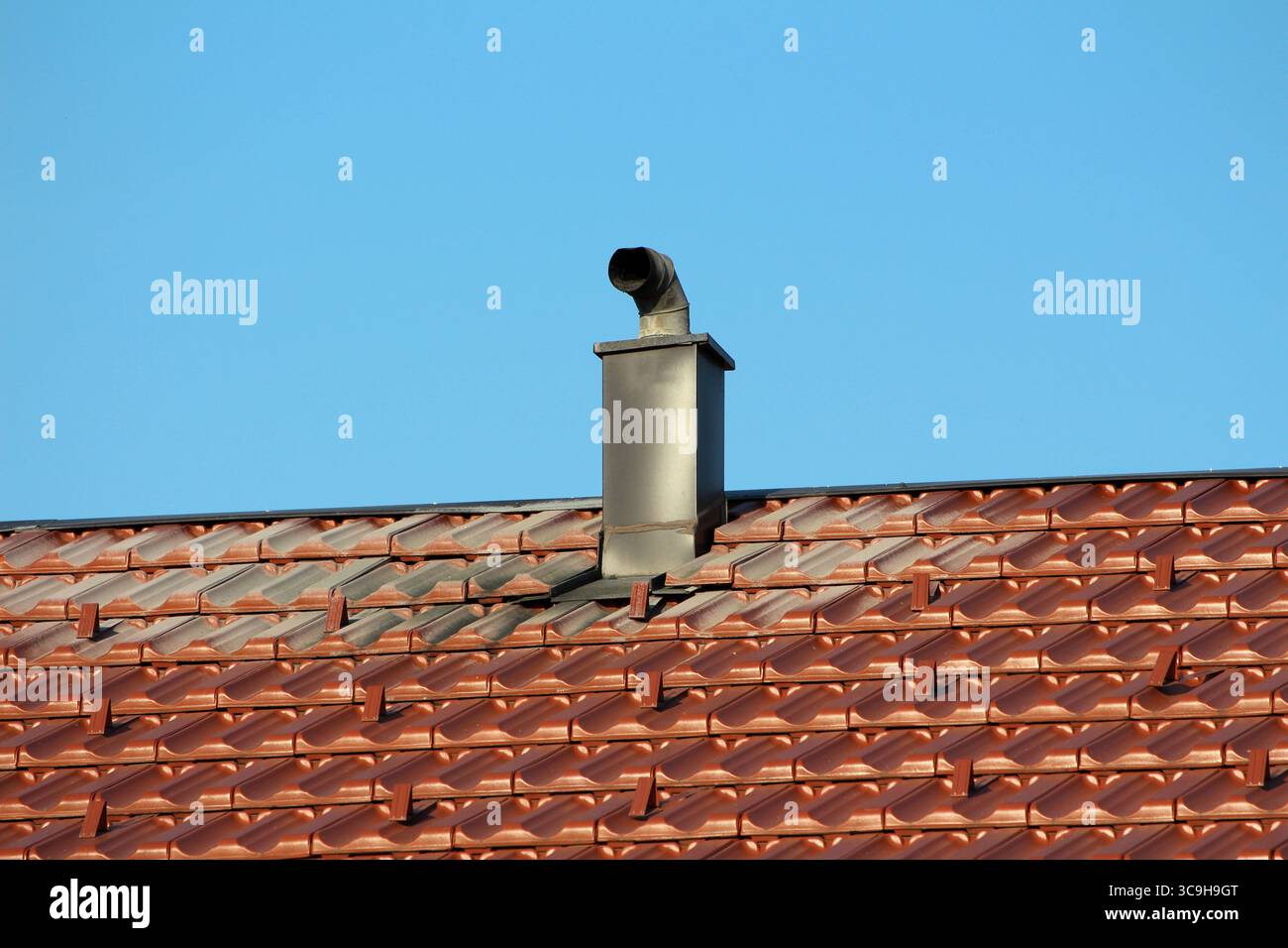 A contemporary metal chimney with a curved outlet rises from a roof of ...