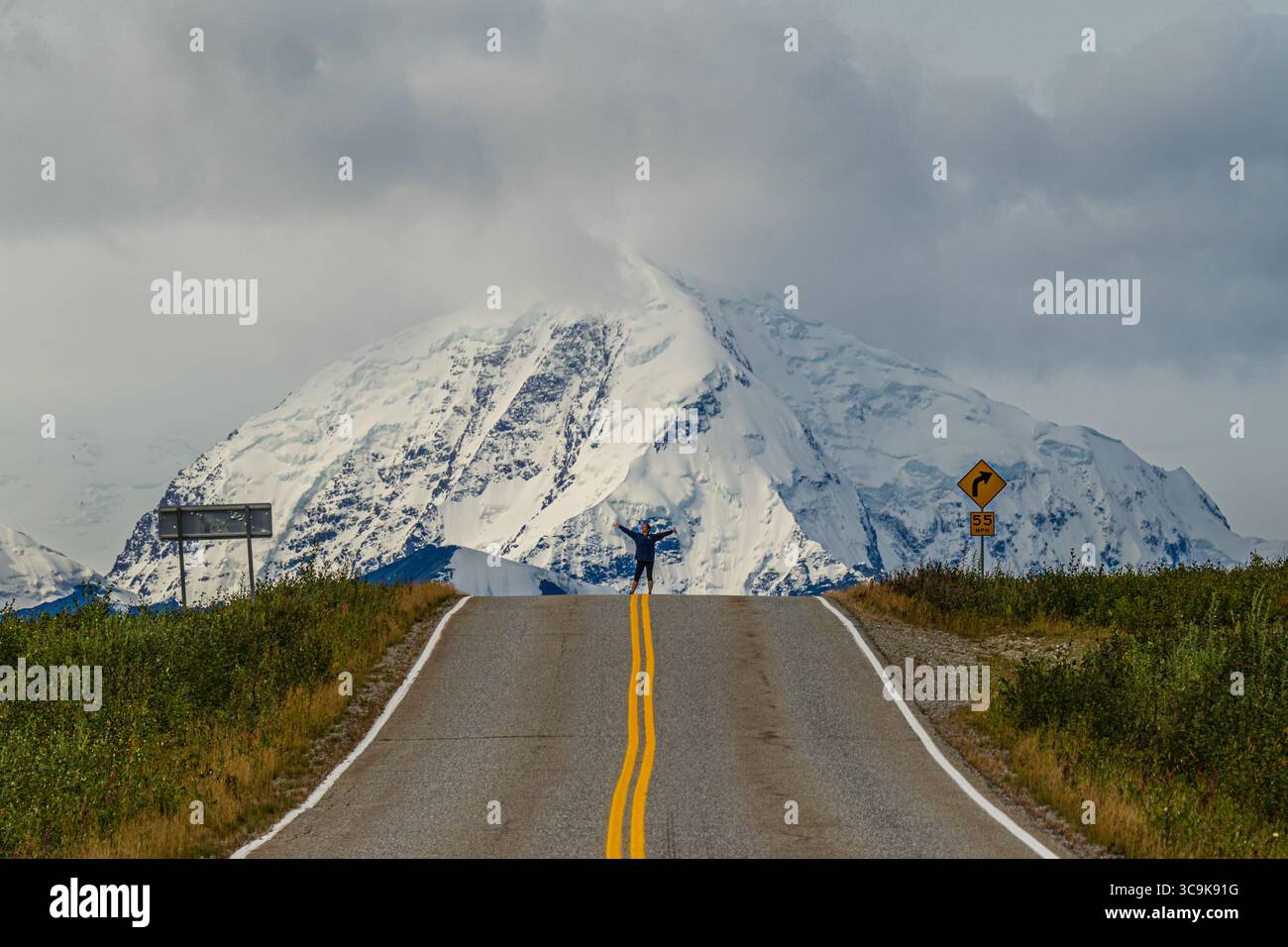 A tourist stands on the road to capture the grandeur of Denali, North ...