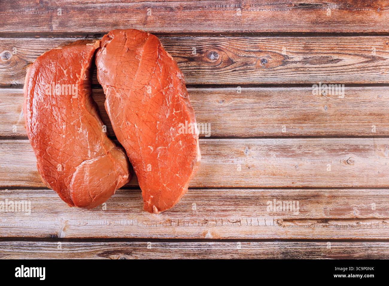 Two raw beef steaks are placed side by side on an aged wooden table in ...