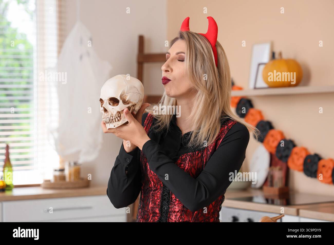 Happy mature woman dressed as devil with human skull blowing kiss in ...