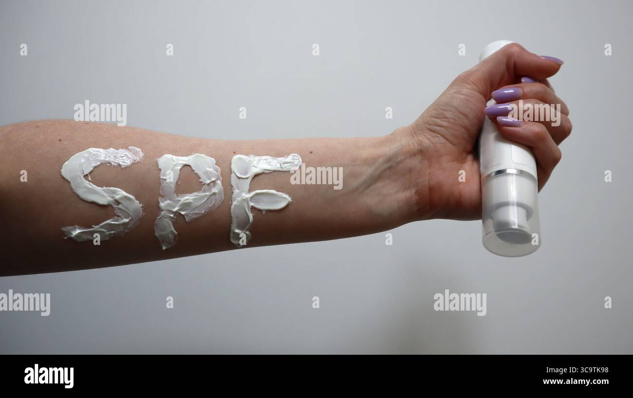 Photo of woman's hand holding jar of sunscreen. On hand is white cream ...