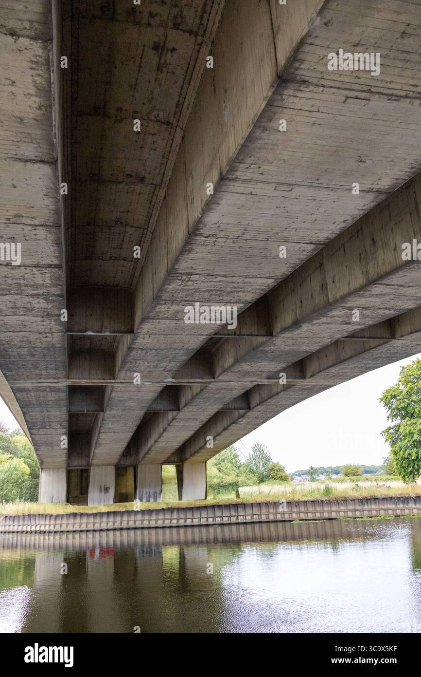 Concrete bridge structure reflected in calm river water, viewed from ...