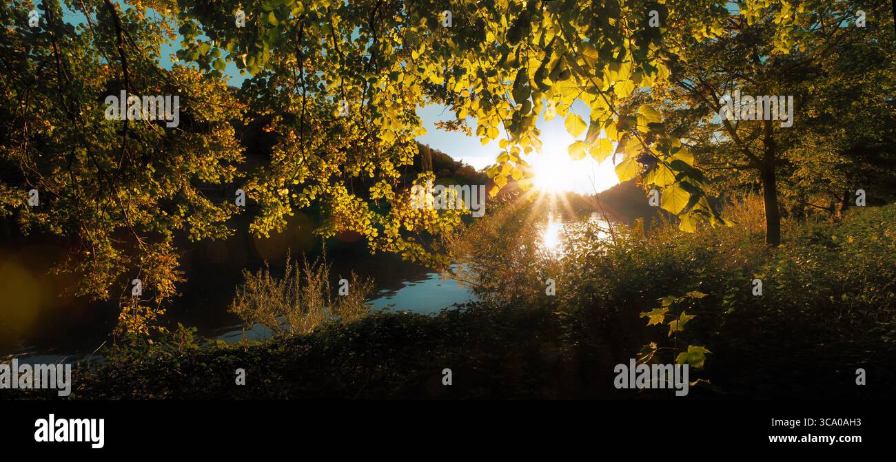Sunset at a river viewed through beautiful lush autumn foliage ...