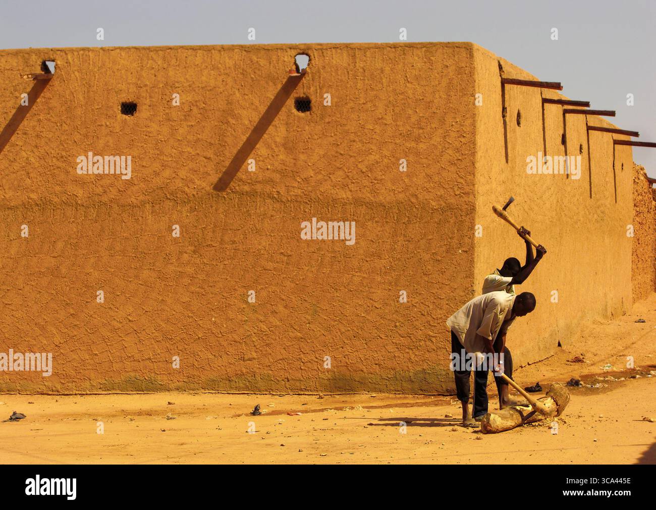 Two men in Agadez, Niger, work under the sun breaking wood near a ...