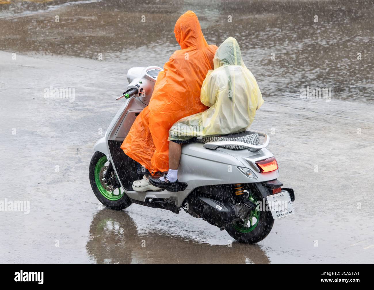 A person with a girl in school uniform ride in the rain on a motorcycle ...