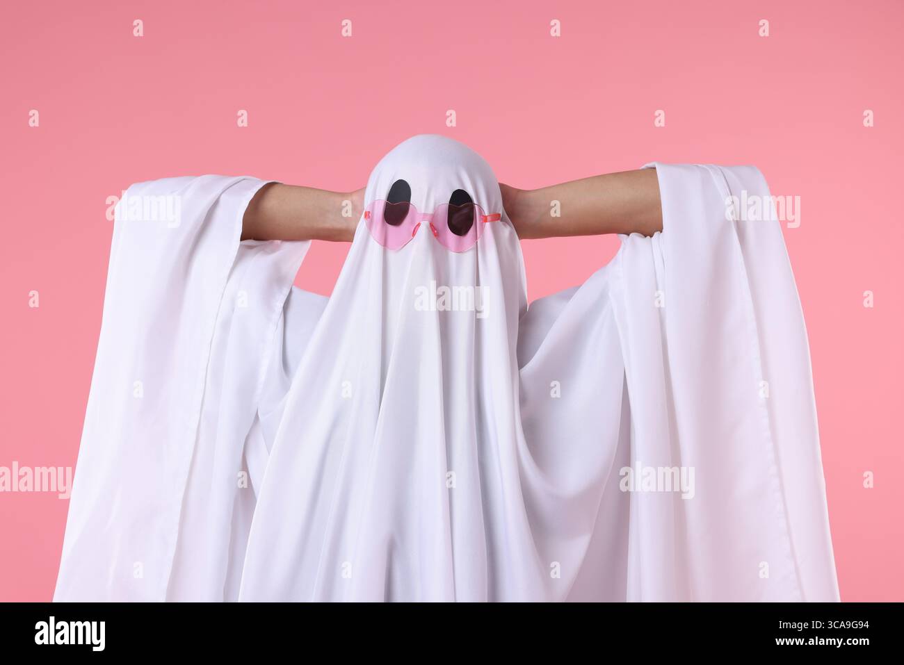 Cute ghost. Man covered with white sheet in sunglasses on pink ...