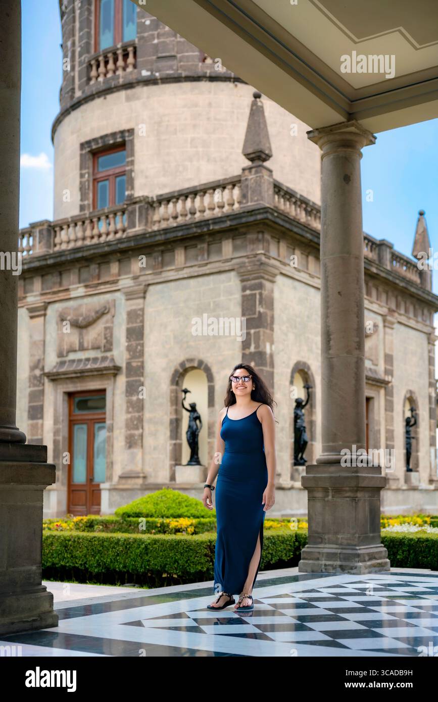 Young happy Latina woman in a fitted blue dress and sunglasses stands ...