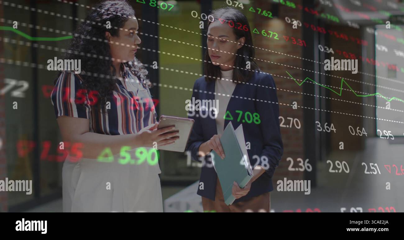 Comparing stock charts on tablet and folder by businesswomen in office ...