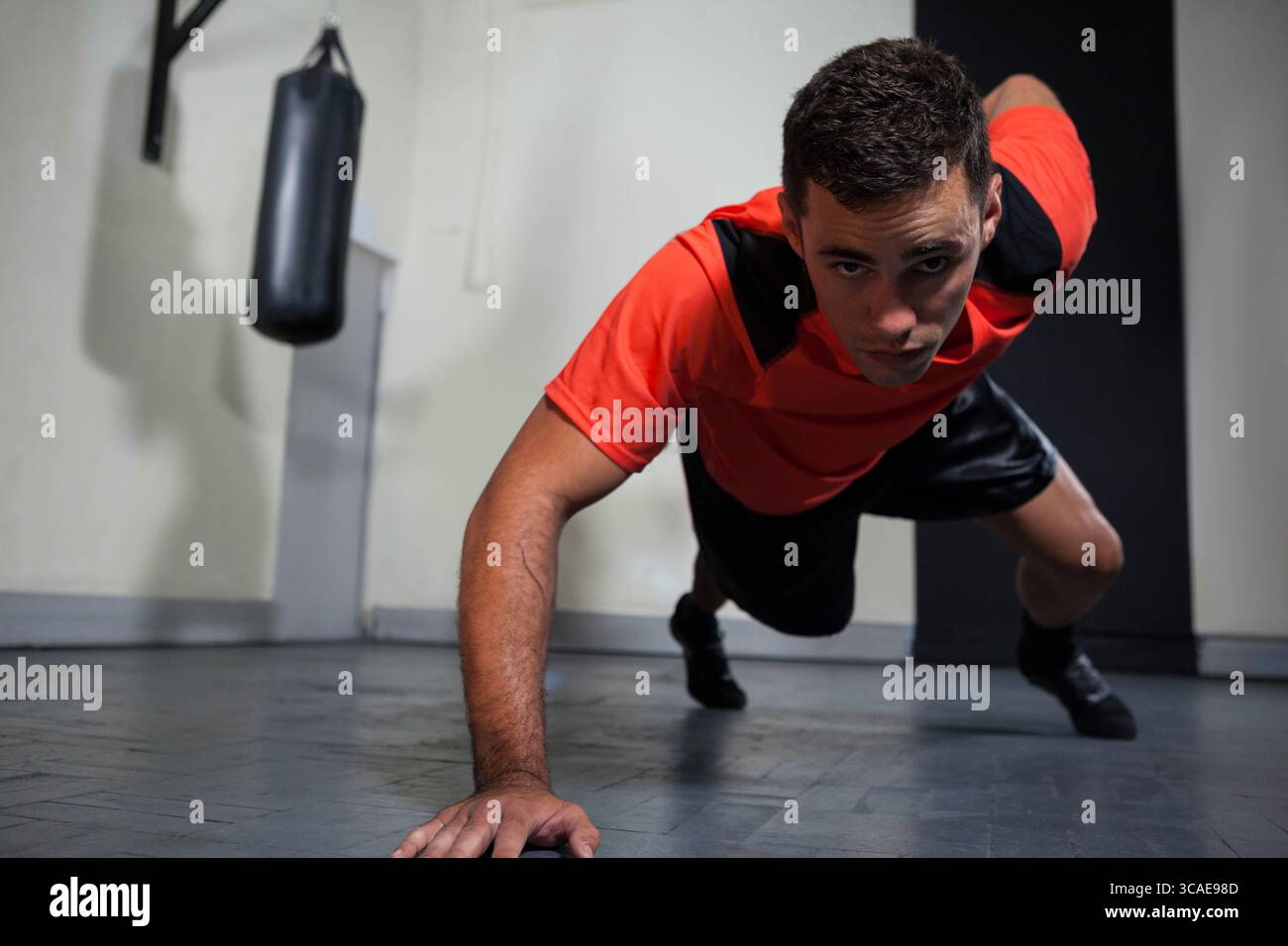 Male in red shirt performing one-arm pushup on rubber gym floor with ...