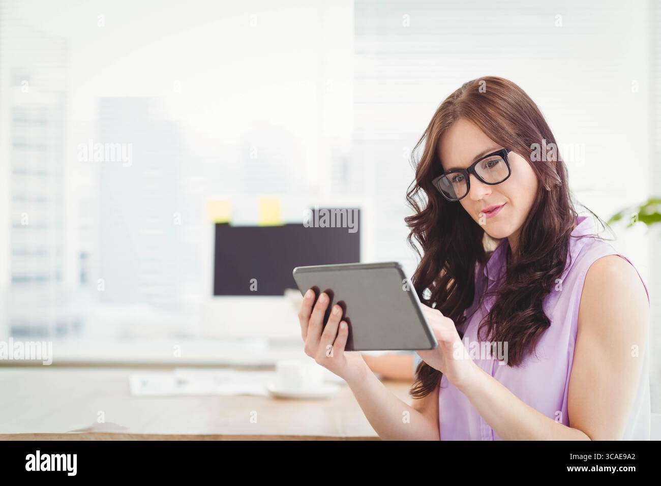 Woman holding tablet and gazing at screen at wooden desk in modern ...