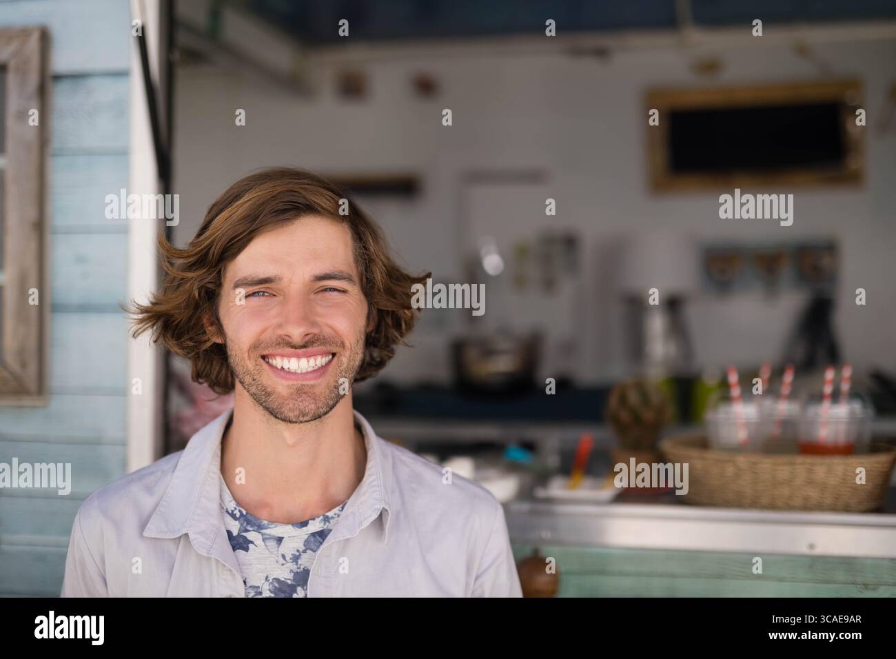 Mid adult man smiling behind pastel blue counter at cafe with blender ...