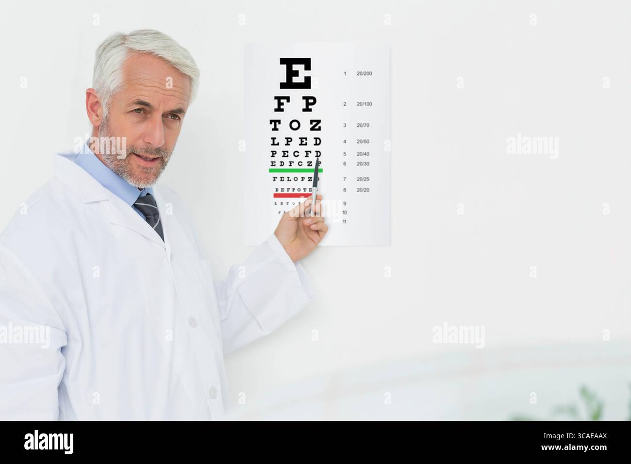 Senior male optometrist holding pointer and pointing at Snellen eye ...