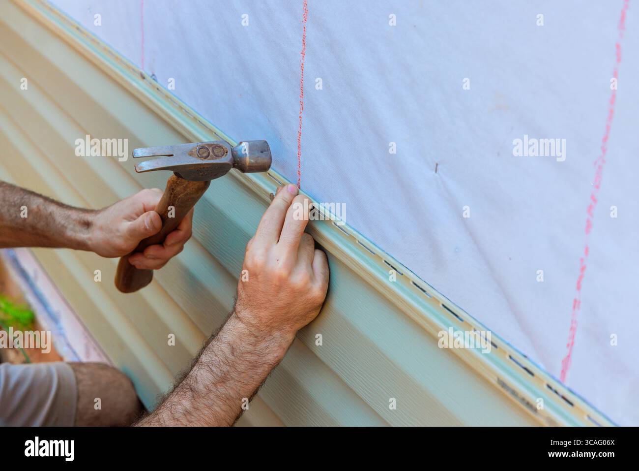 Contractor is using hammer to secure facade vinyl siding plank on ...